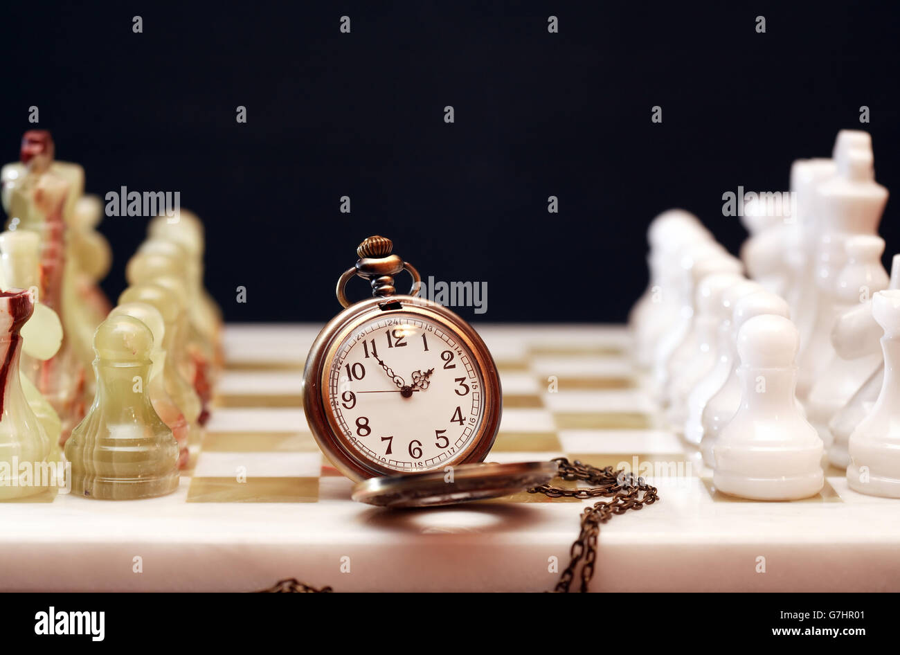Set of chess pieces made from Onyx near watch on board against dark ...