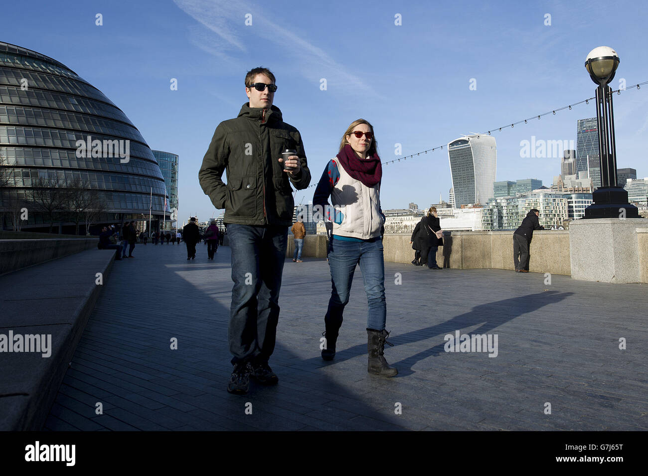 Walkers wrap up as they stroll along the South Bank in central London ...
