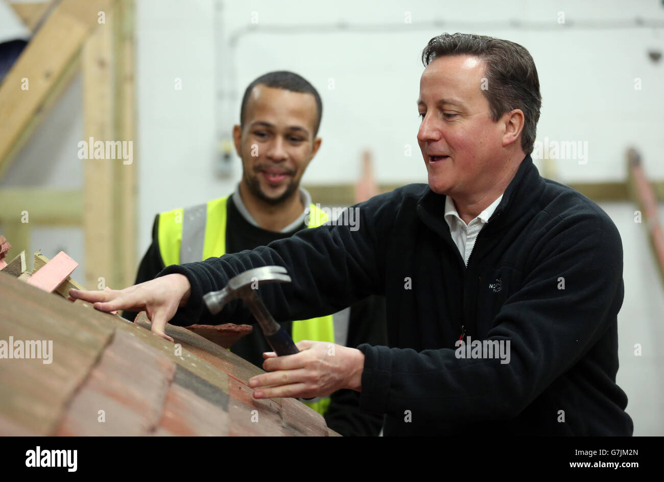Prime Minister David Cameron fixes tiles to a roof mockup, alongside ...