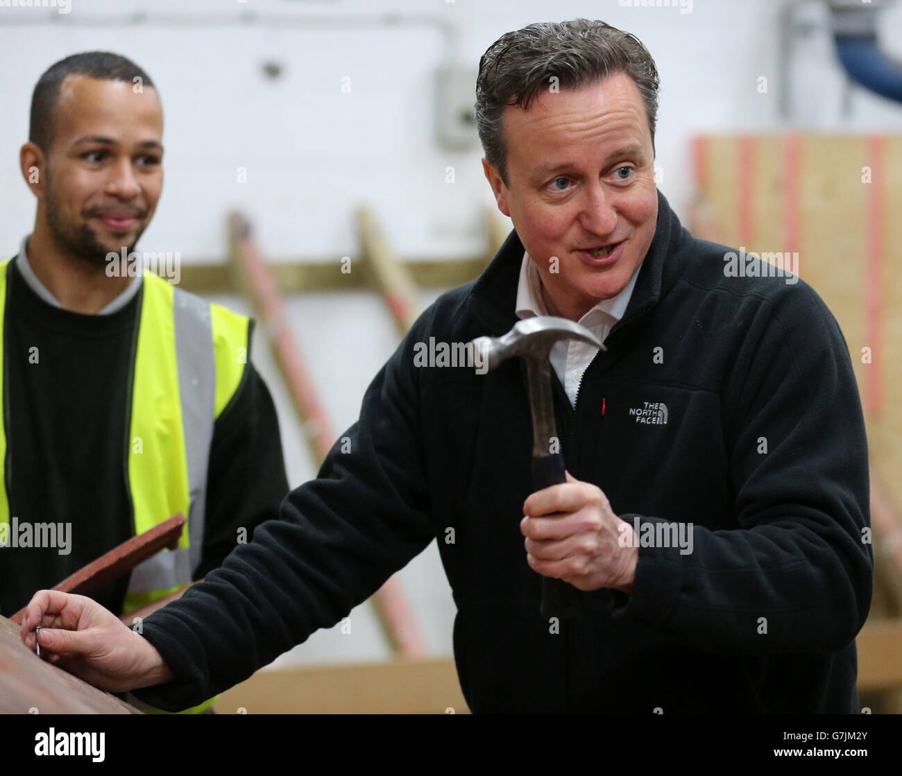 Prime Minister David Cameron fixes tiles to a roof mockup, alongside ...