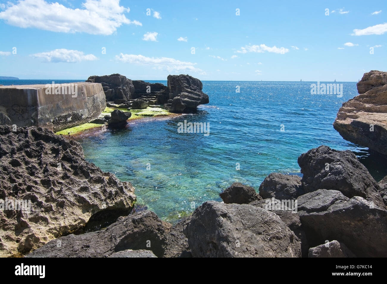 Rocky landscape with green seagrass, water and concrete pier on a sunny ...