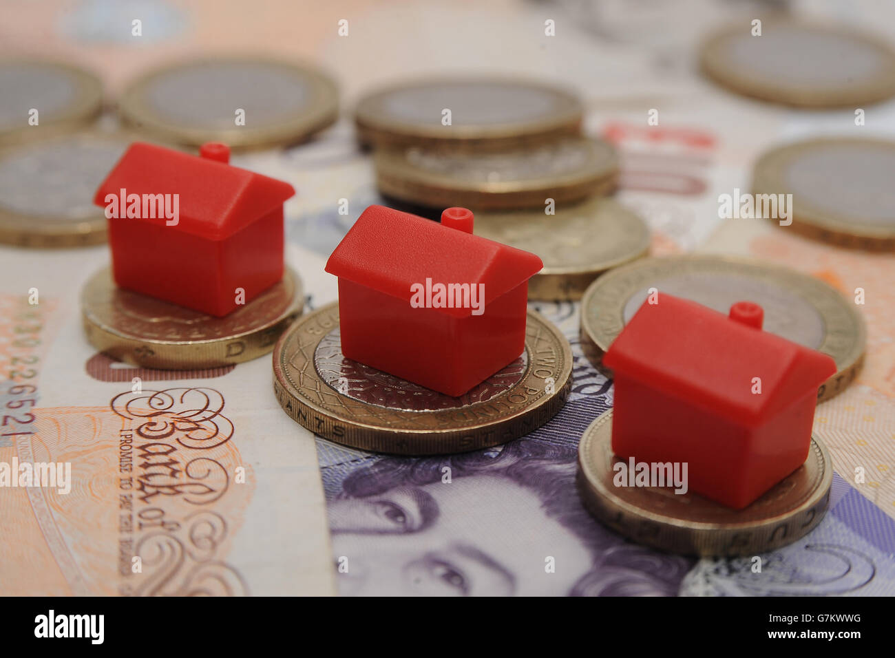 Plastic models of houses sit on a pile of coins and bank notes Stock ...