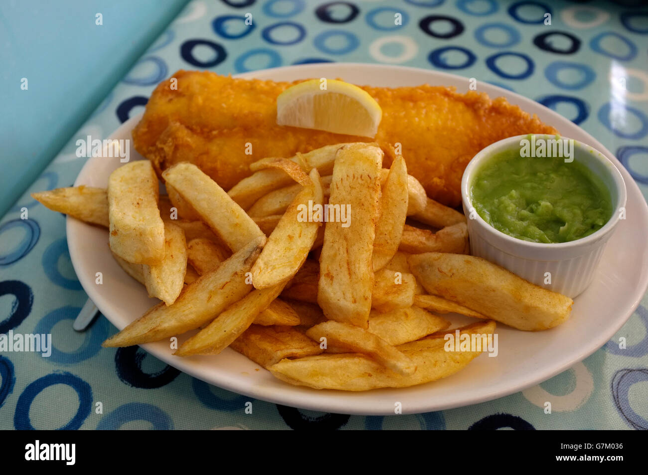 cod fish and chips with mushy peas displaid on a china plate in ...