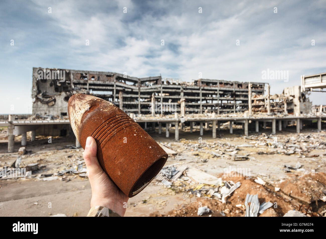 Unexploded 120 mm shell in hand with airport ruins Stock Photo - Alamy