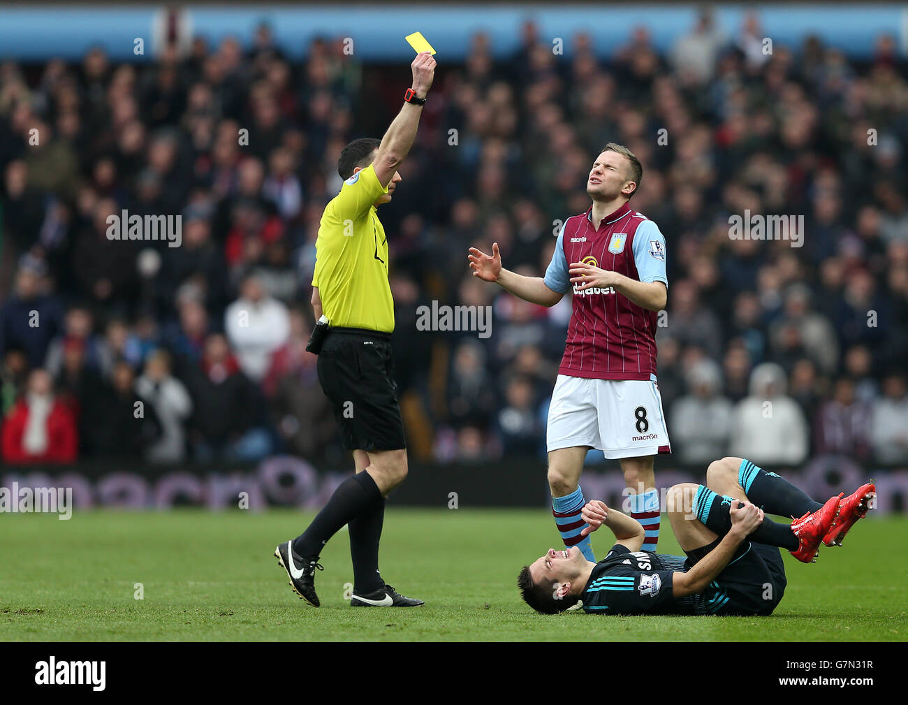 Referee Neil Swarbrick (left) shows a yellow card to Aston Villa's Tom ...