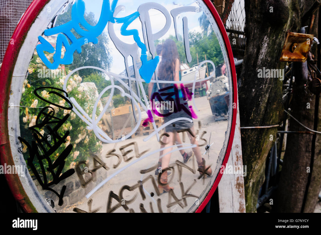 People walk past an outdoor security mirror, covered with graffiti ...