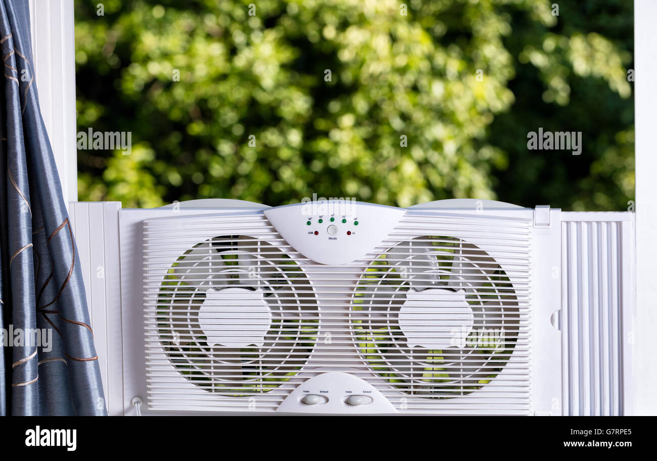 Two way window fan in home window with blurred out trees in background ...