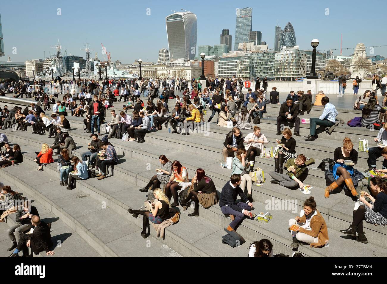 A large crowd of city workers enjoy their lunch break in the warm ...
