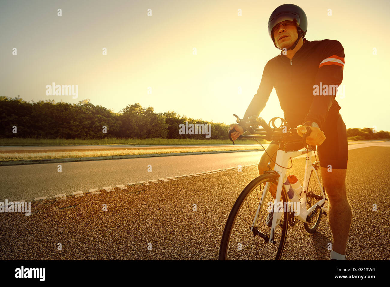 Sun rises behind man getting ready to ride his road bike on lonely ...