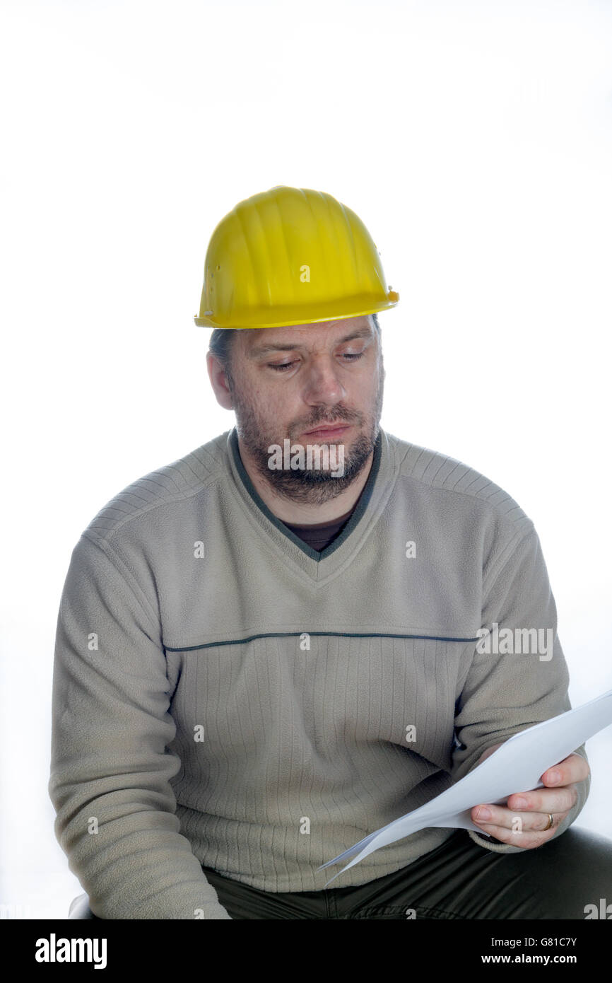 Young construction engineer wearing a yellow helmet reads a ...