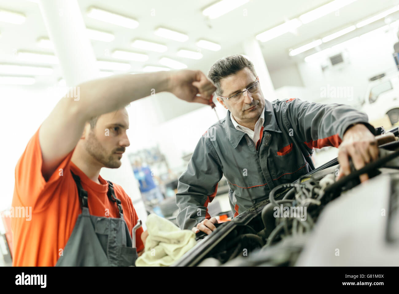 Car mechanics fixing car in garage - teamwork Stock Photo - Alamy