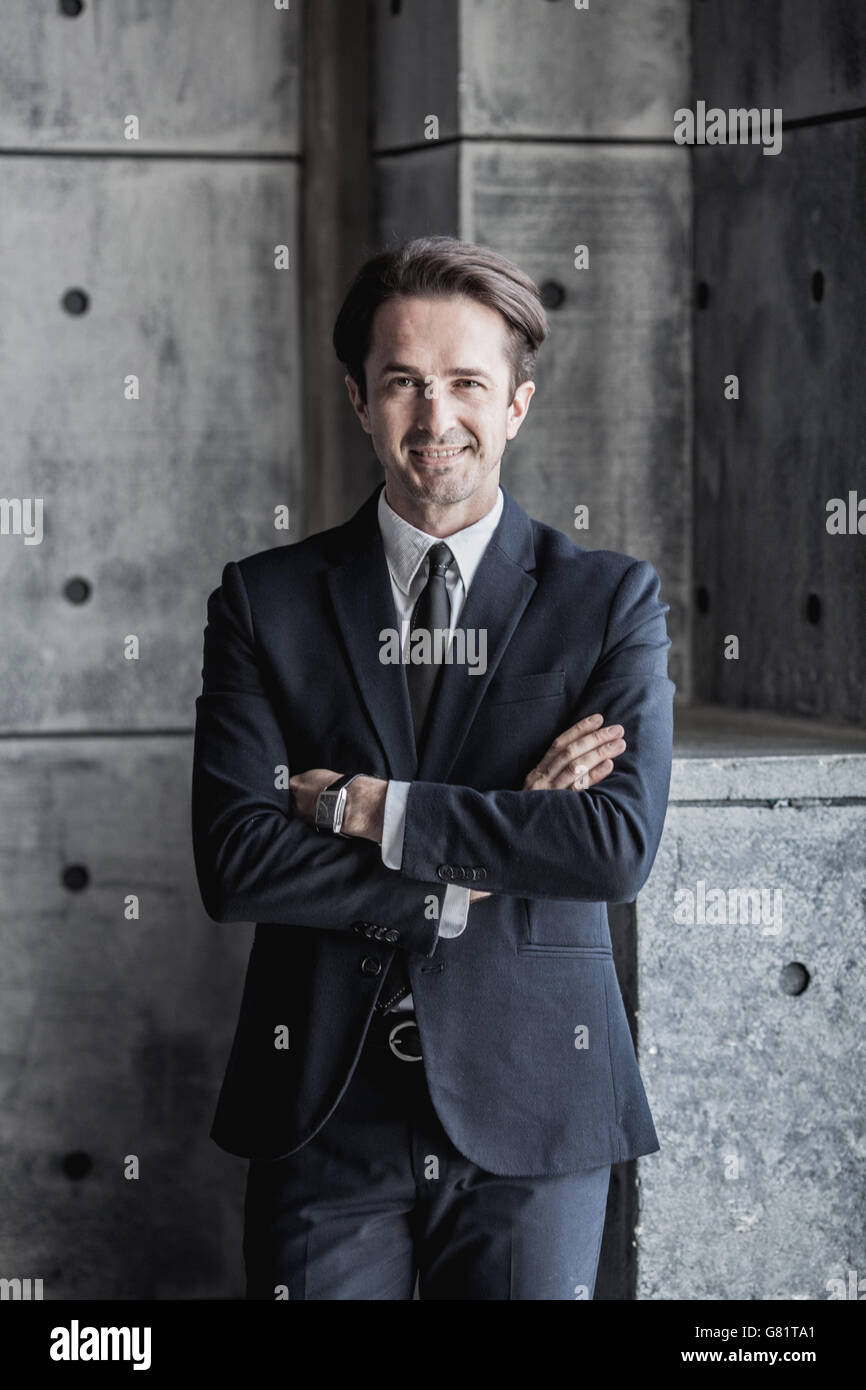 Portrait of smiling businessman in suit over concrete wall background ...