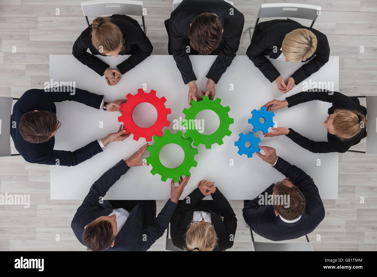 Business team sitting around the table with cogs, teamwork concept ...