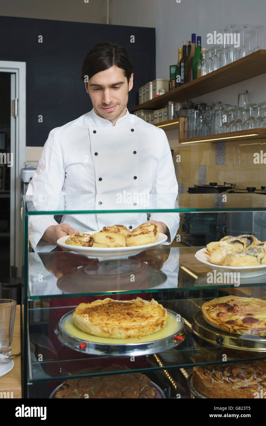 Chef arranging food on glass shelf for retail display at cafe Stock ...