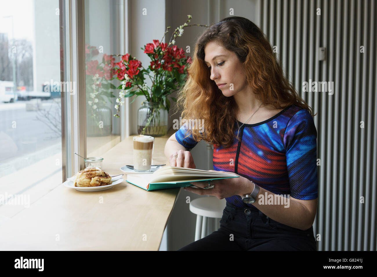 Young woman reading book while having breakfast at cafe Stock Photo - Alamy