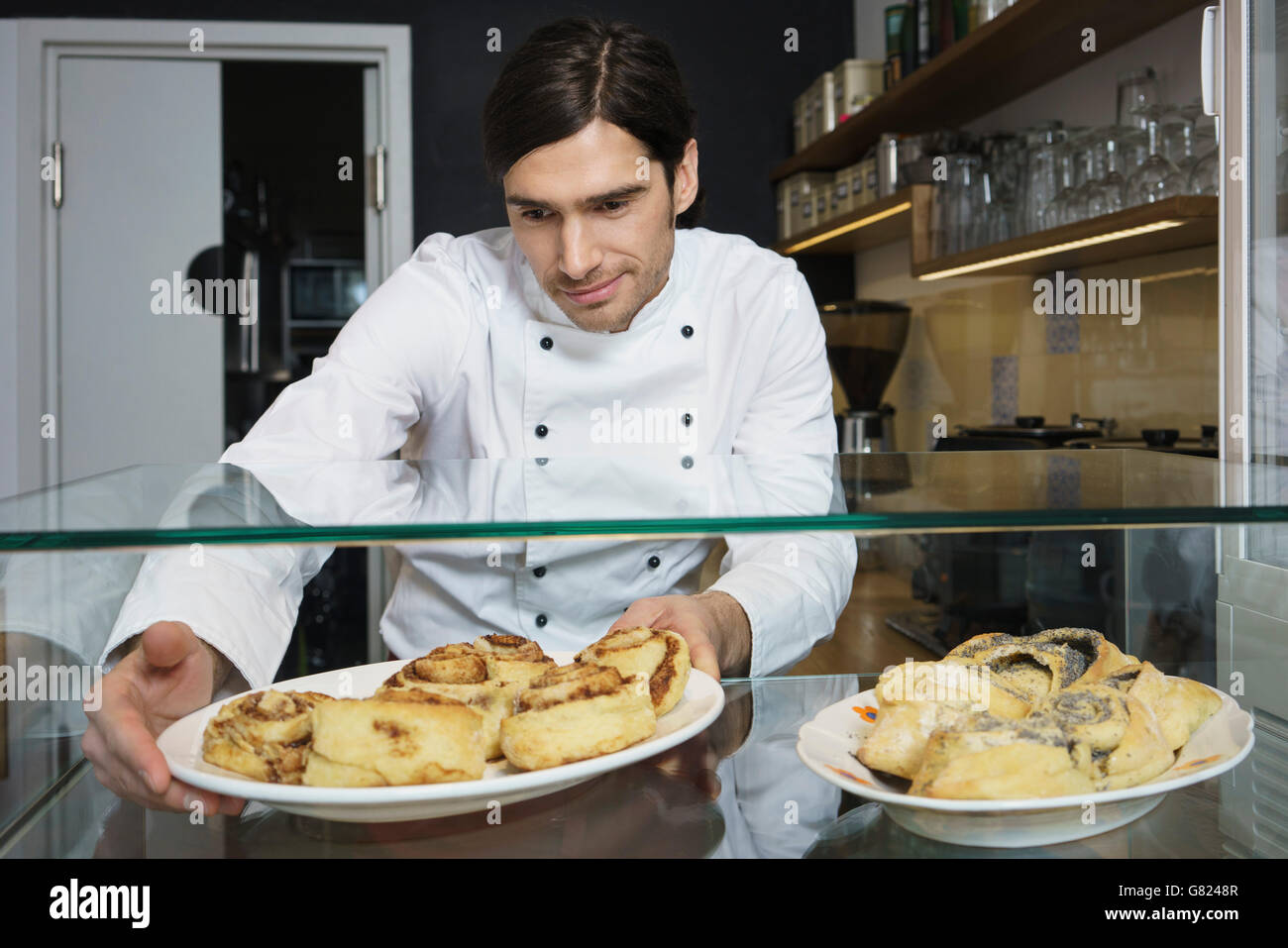 Male chef keeping cinnamon rolls for retail display at cafe Stock Photo ...