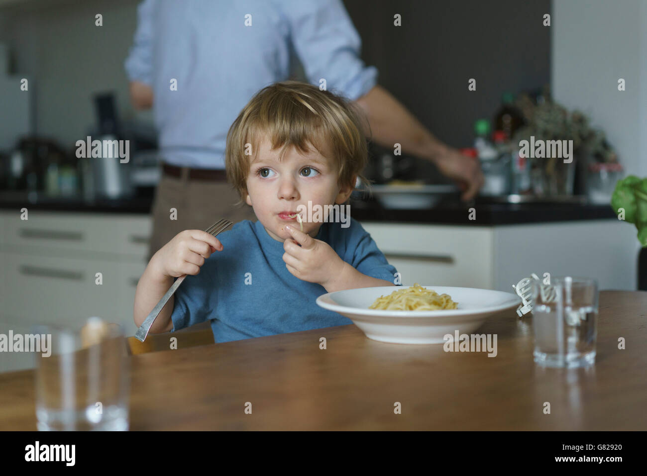 Boy eating noodles while father working in kitchen at home Stock Photo ...
