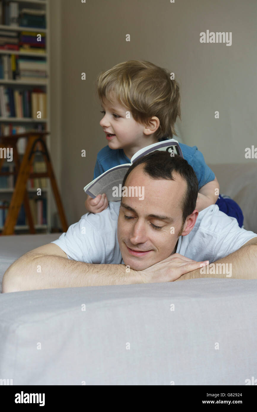 Boy with book sitting on father's back in bedroom Stock Photo - Alamy