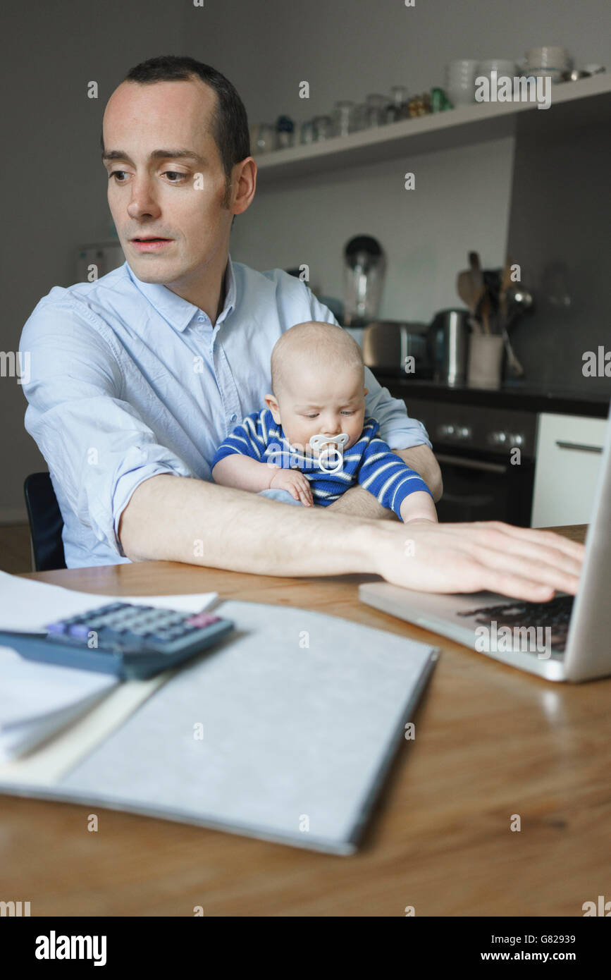 Father carrying son and working on documents at home Stock Photo - Alamy