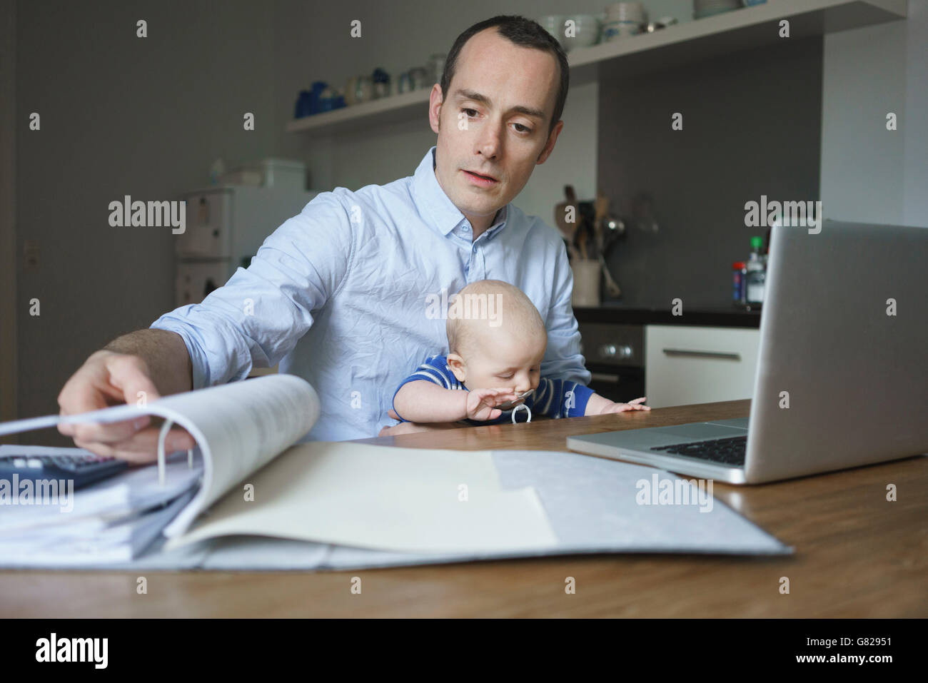 Serious father carrying son and reading documents at home Stock Photo ...