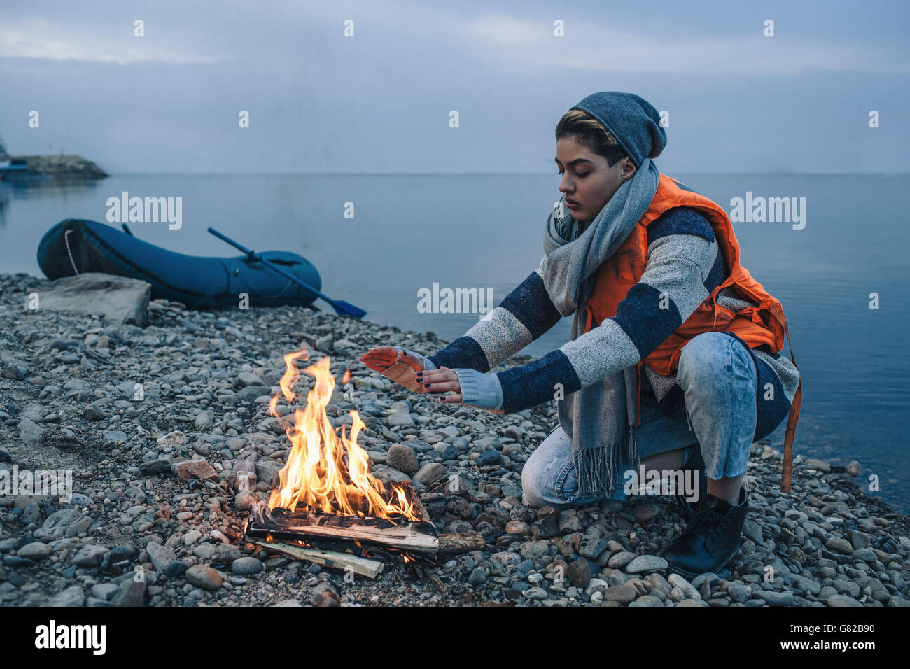 Full length of teenage girl warming hands over bonfire on lakeshore ...