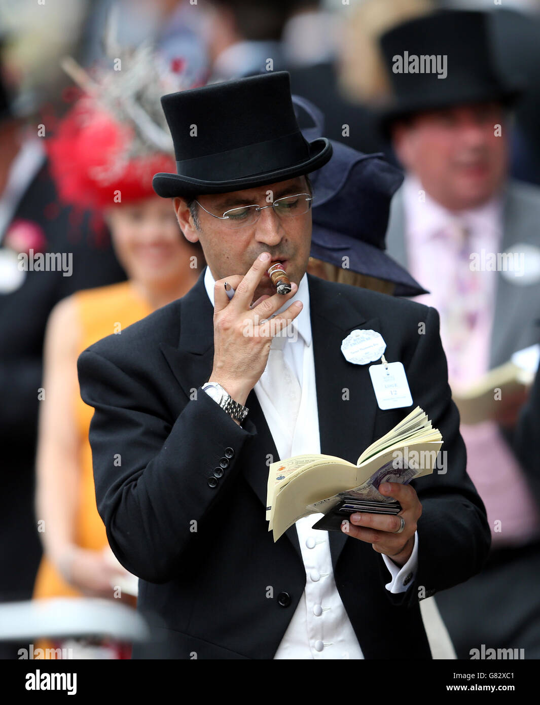 A racegoer smokes a cigar as he checks the race card on day two of the ...