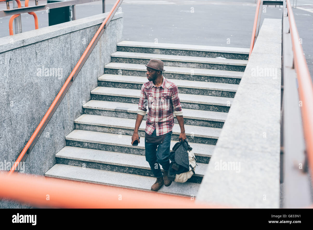 Young handsome afro black man going downstairs to the underground, holding a bag and smartphone ...