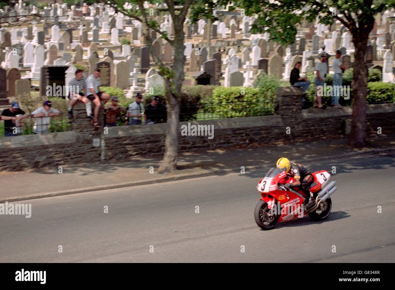 Joey Dunlop rides past a cemetary in the Formula One race Stock Photo ...
