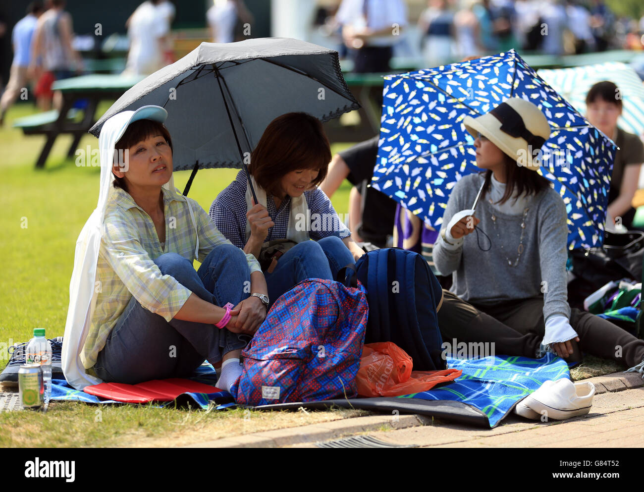 Spectators shield themselves from the sun as they wait in the ticket ...