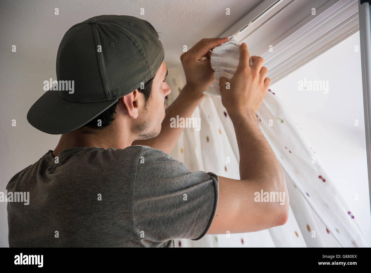 Young handsome man or handyman installing curtains over window at home ...