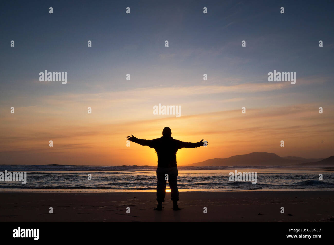 Silhouette of man standing with arms outstretched on beach at sunset ...