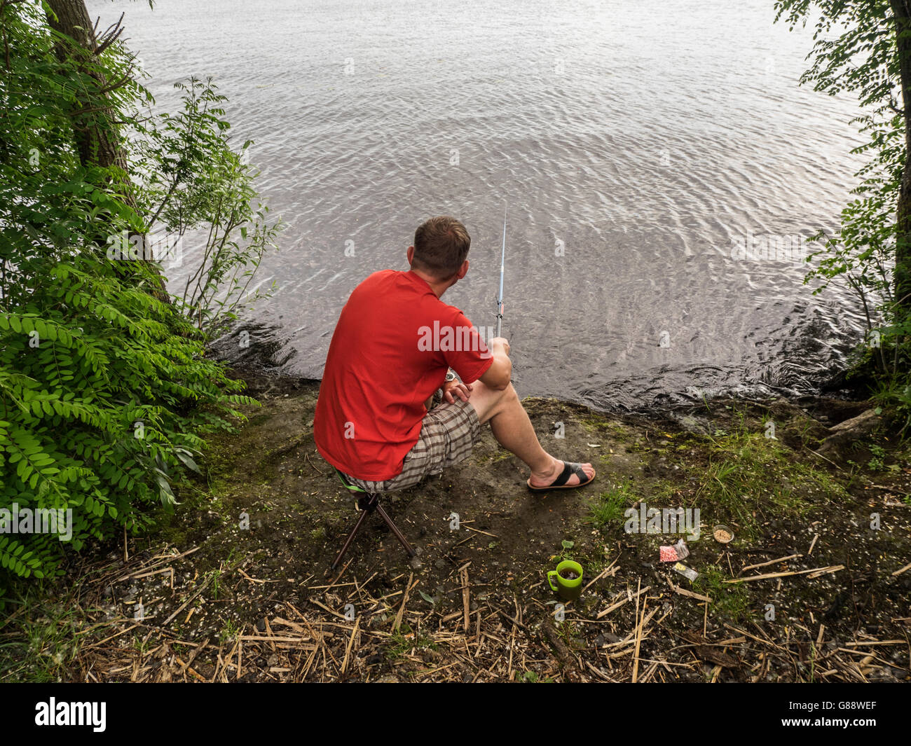 Man sitting by river fishing Stock Photo - Alamy