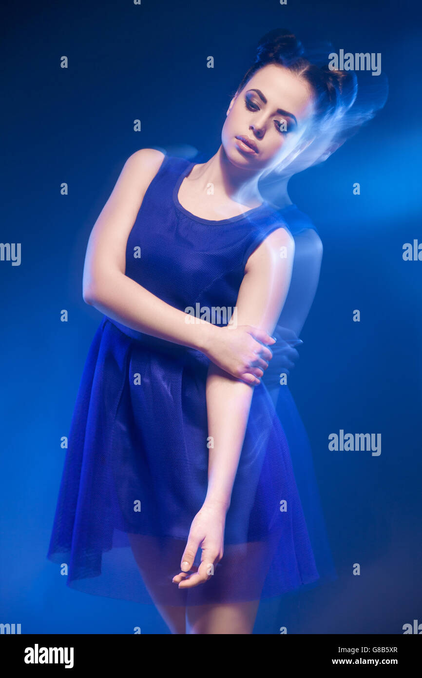 Portrait of beautiful young model posing in blue dress against of blue ...