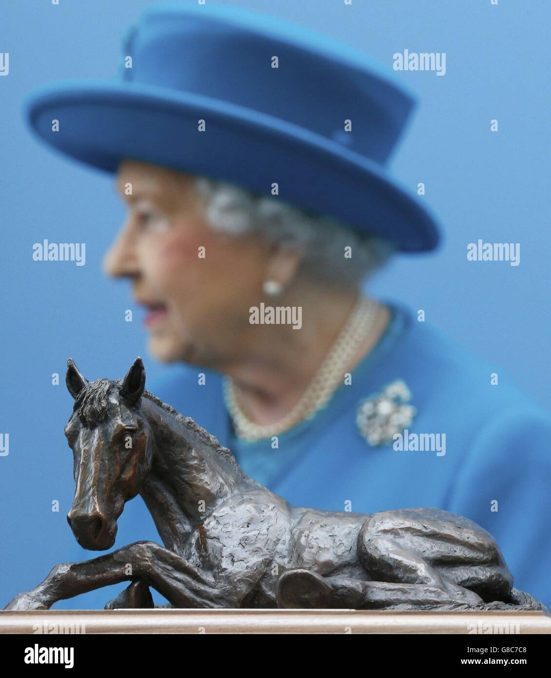 Queen Elizabeth II stands behind a bronze statue of a horse that she ...