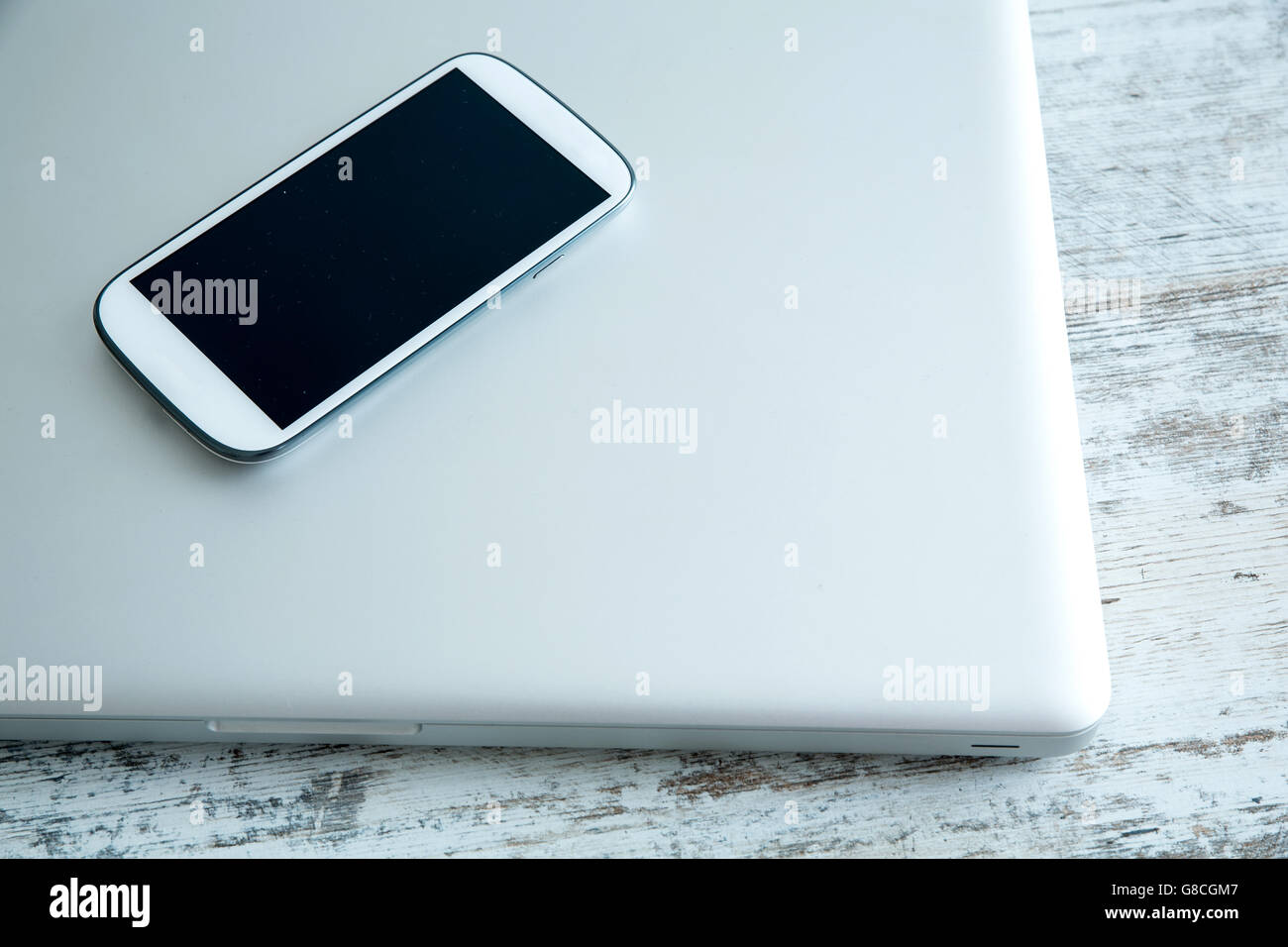 A Smartphone and a switched off laptop computer on a wooden Desktop ...