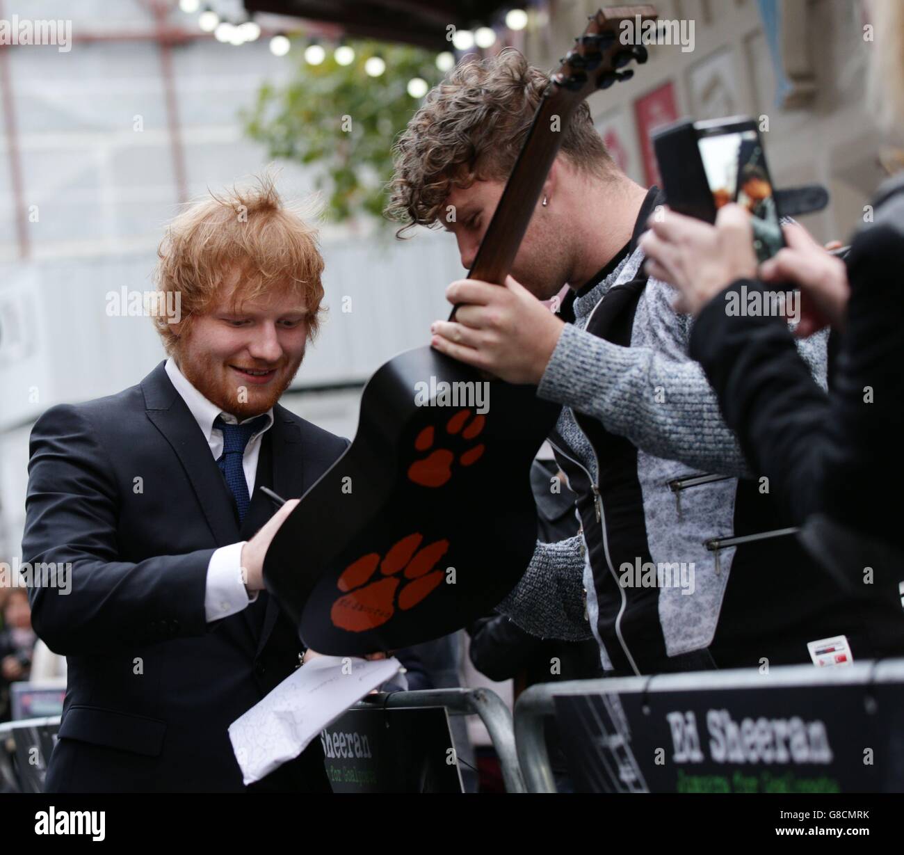 Singer Ed Sheeran signs a guitar as he arrives for the world premiere ...