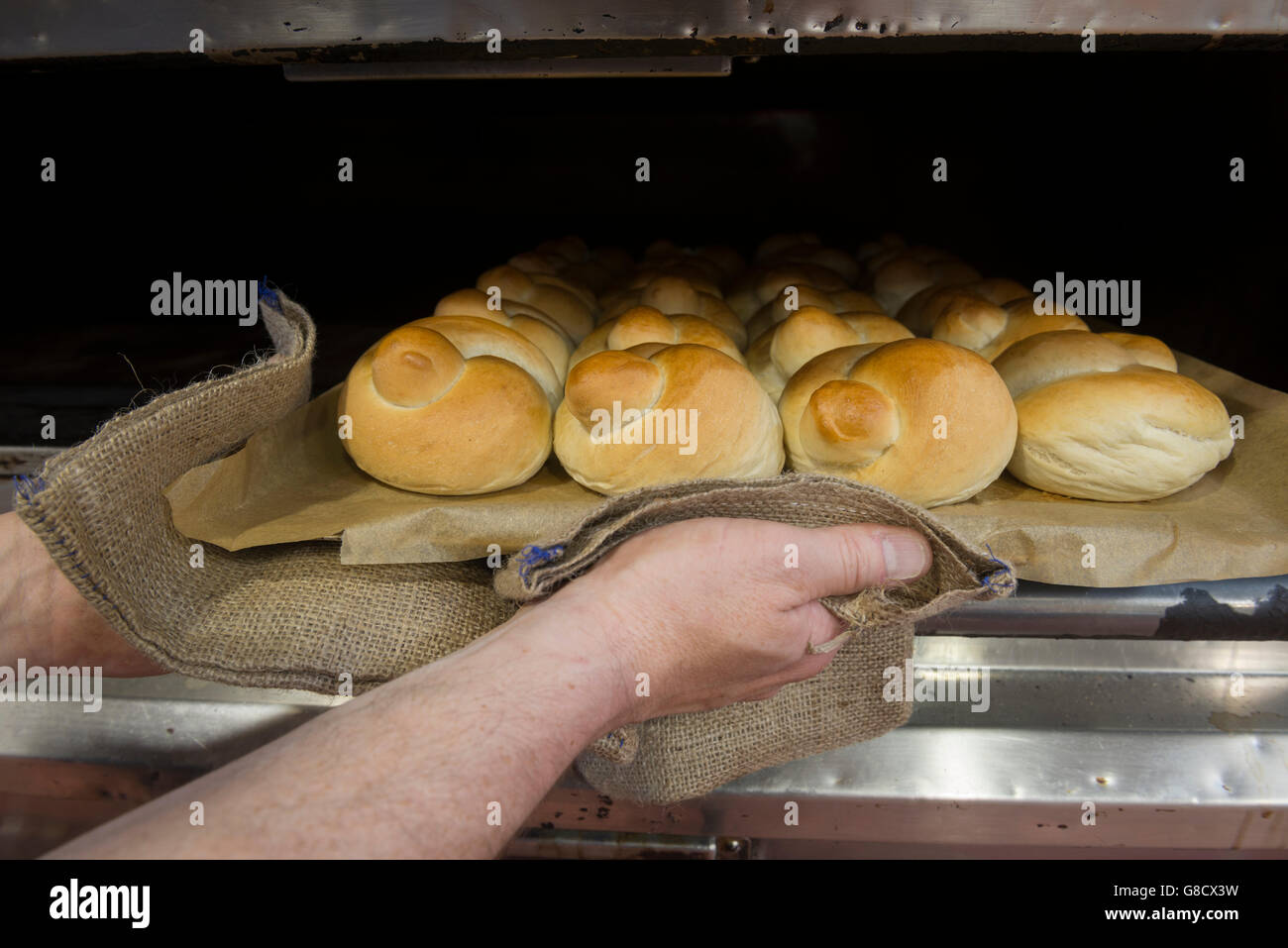 Baker removing freshly baked bread rolls from the oven. England Stock ...