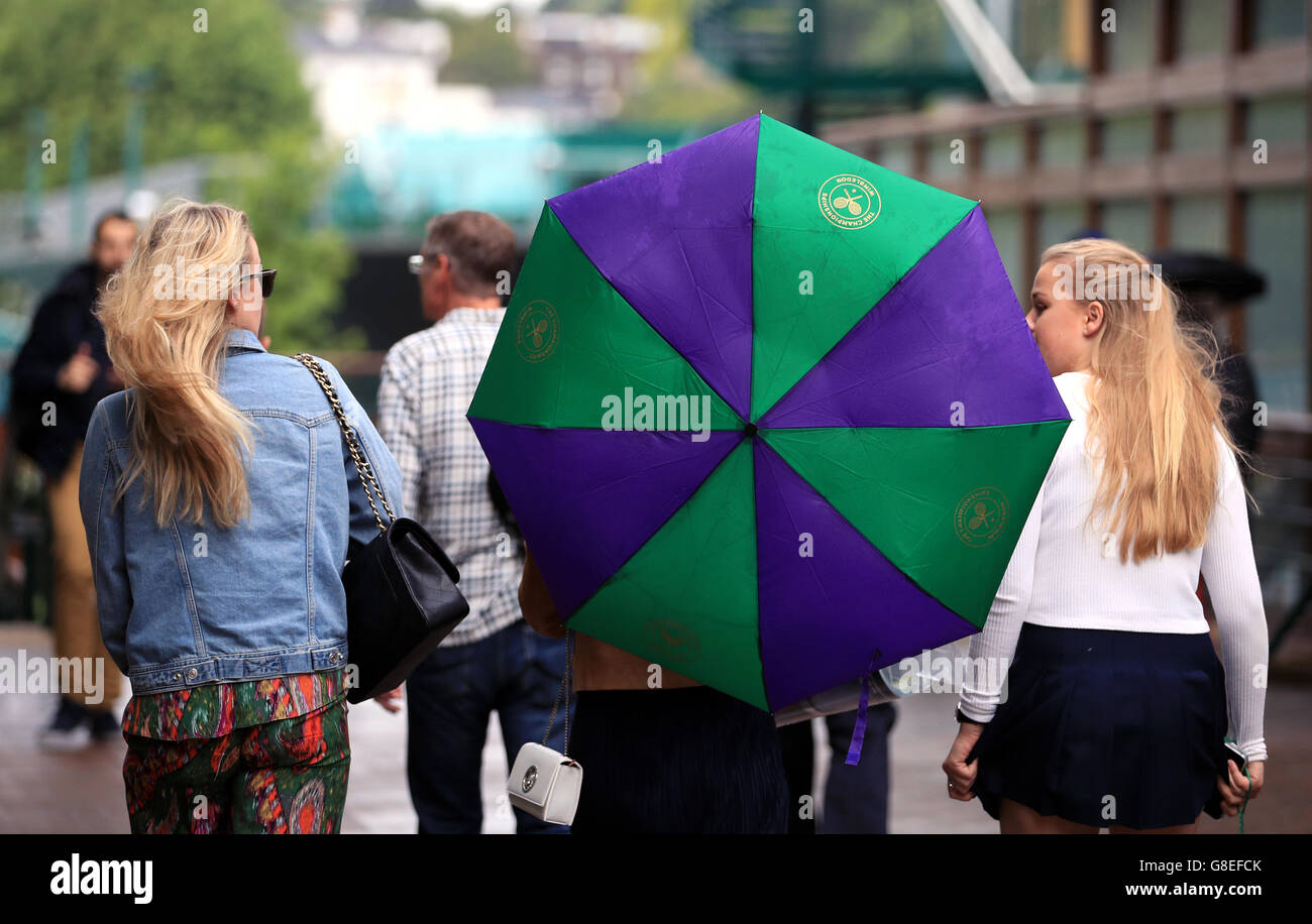 Spectators shelter from the rain under a Wimbledon branded umbrella on ...
