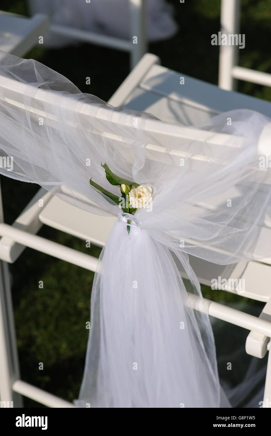 White chair with a small flower. White decorated chairs on a green lawn ...
