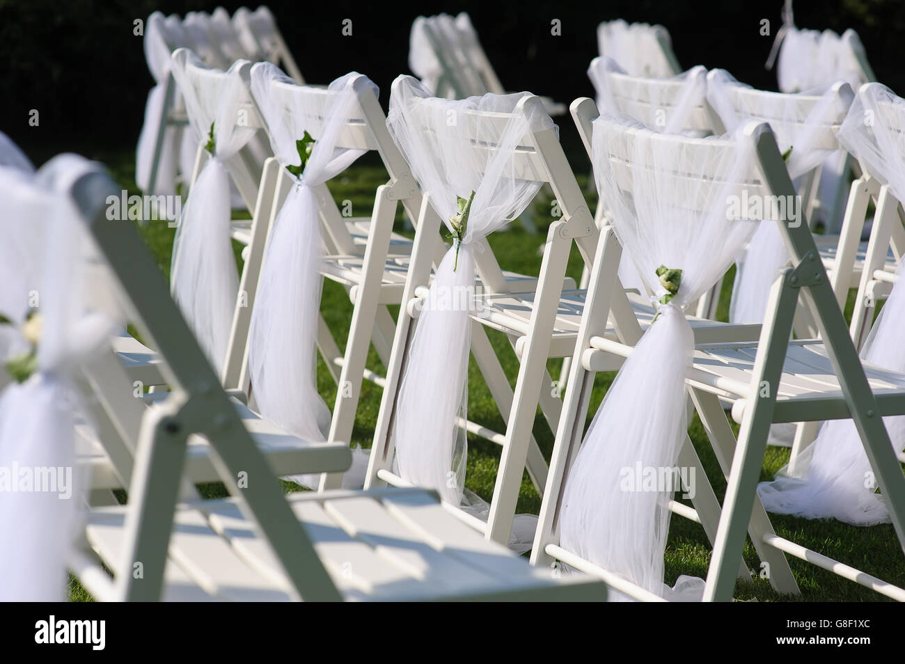 White chair with a small flower. White decorated chairs on a green lawn ...