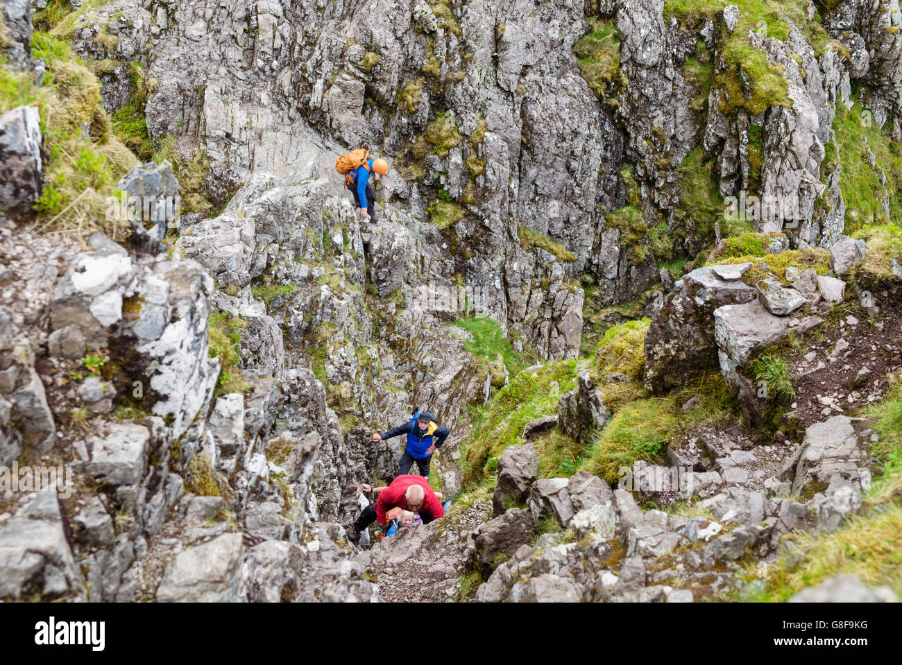 Hikers scrambling on steep rocky pinnacles of Aonach Eagach ridge ...