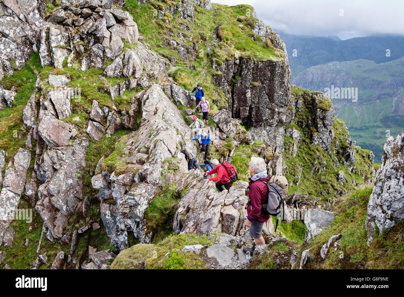 Hikers scrambling on steep rocky pinnacles of Aonach Eagach ridge ...
