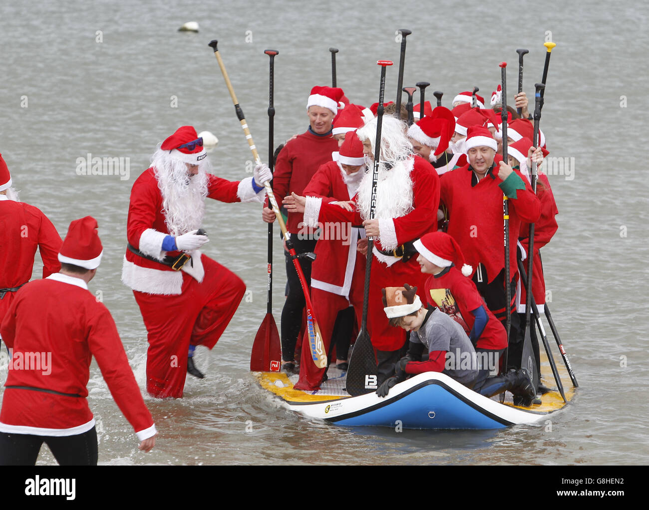 Competitors dressed as Santa Claus take part in a stand up paddle board ...