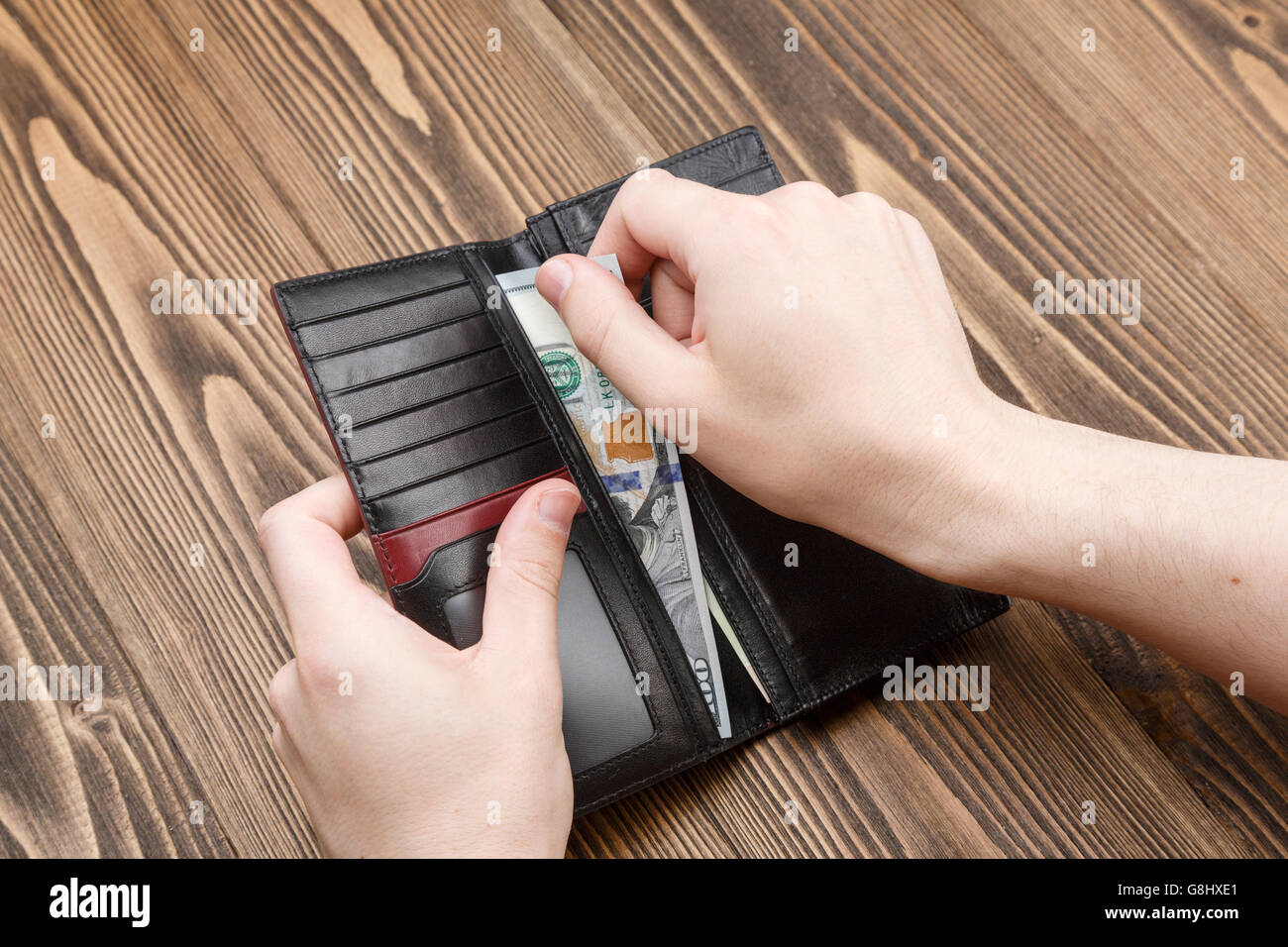 man is putting 100 dollar banknote in a black leather wallet over dark ...