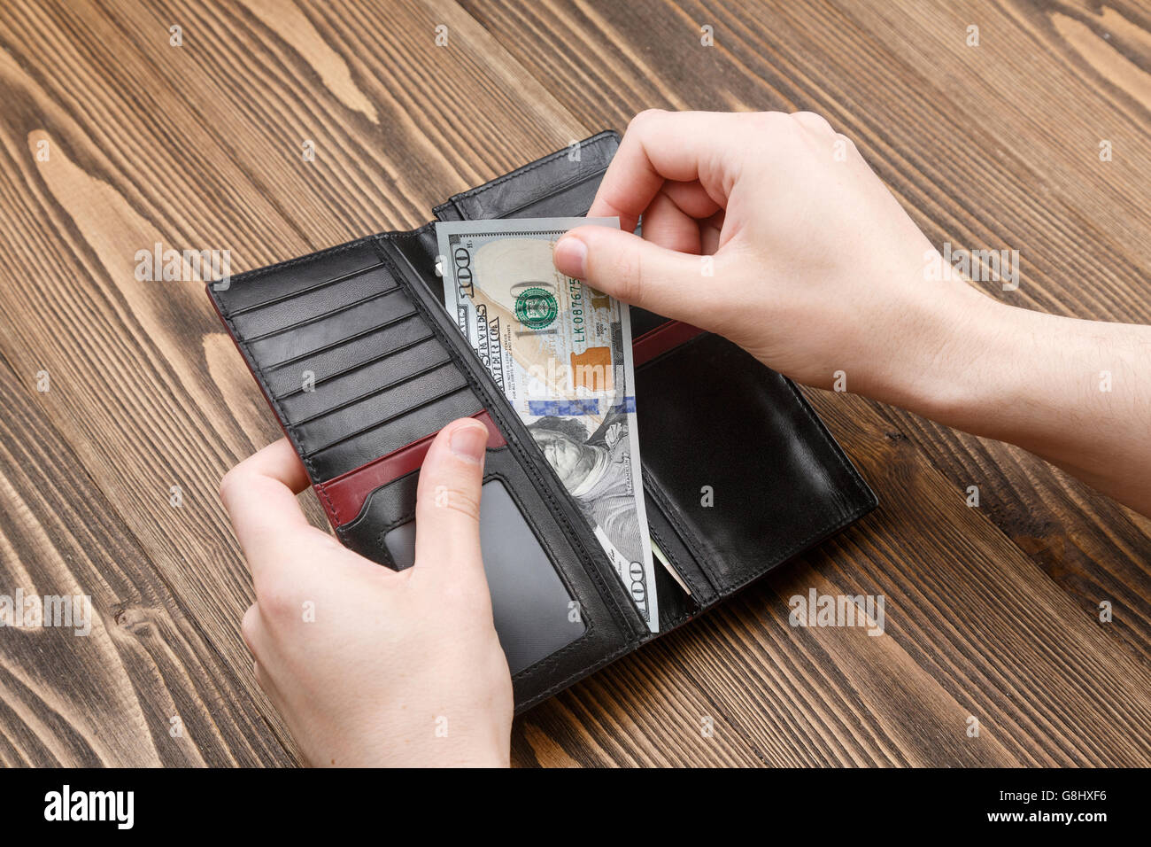 man is putting 100 dollar banknote in a black leather wallet over dark ...
