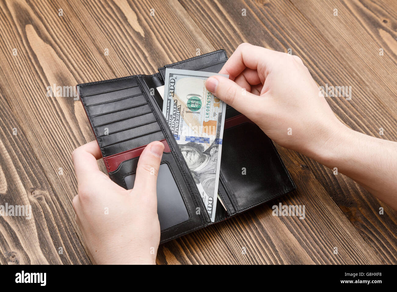 man is putting 100 dollar banknote in a black leather wallet over dark ...