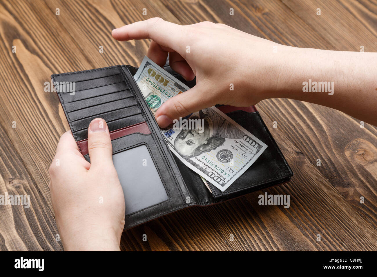 man is putting 100 dollar banknote in a black leather wallet over dark ...