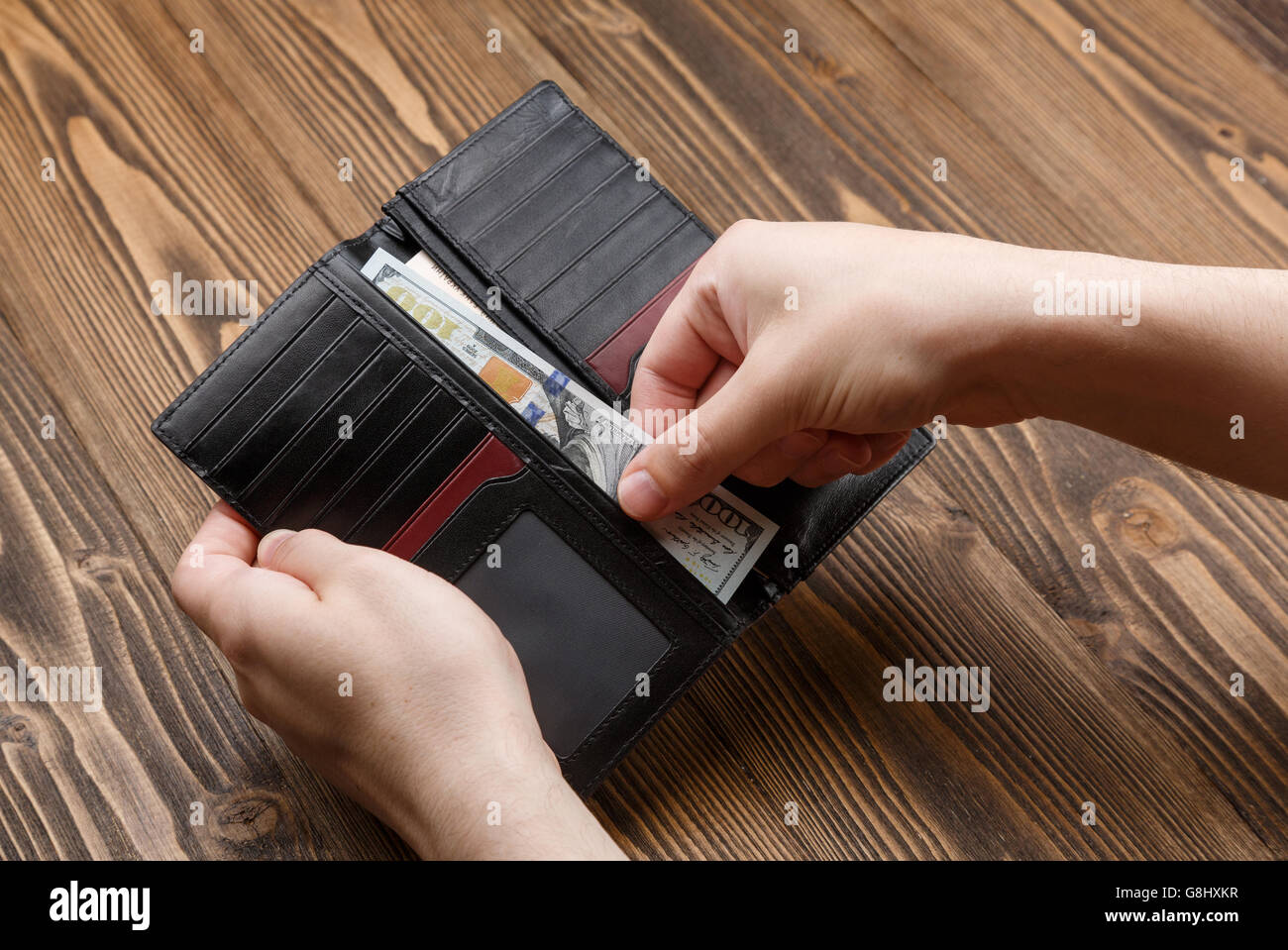 man is putting 100 dollar banknote in a black leather wallet over dark ...