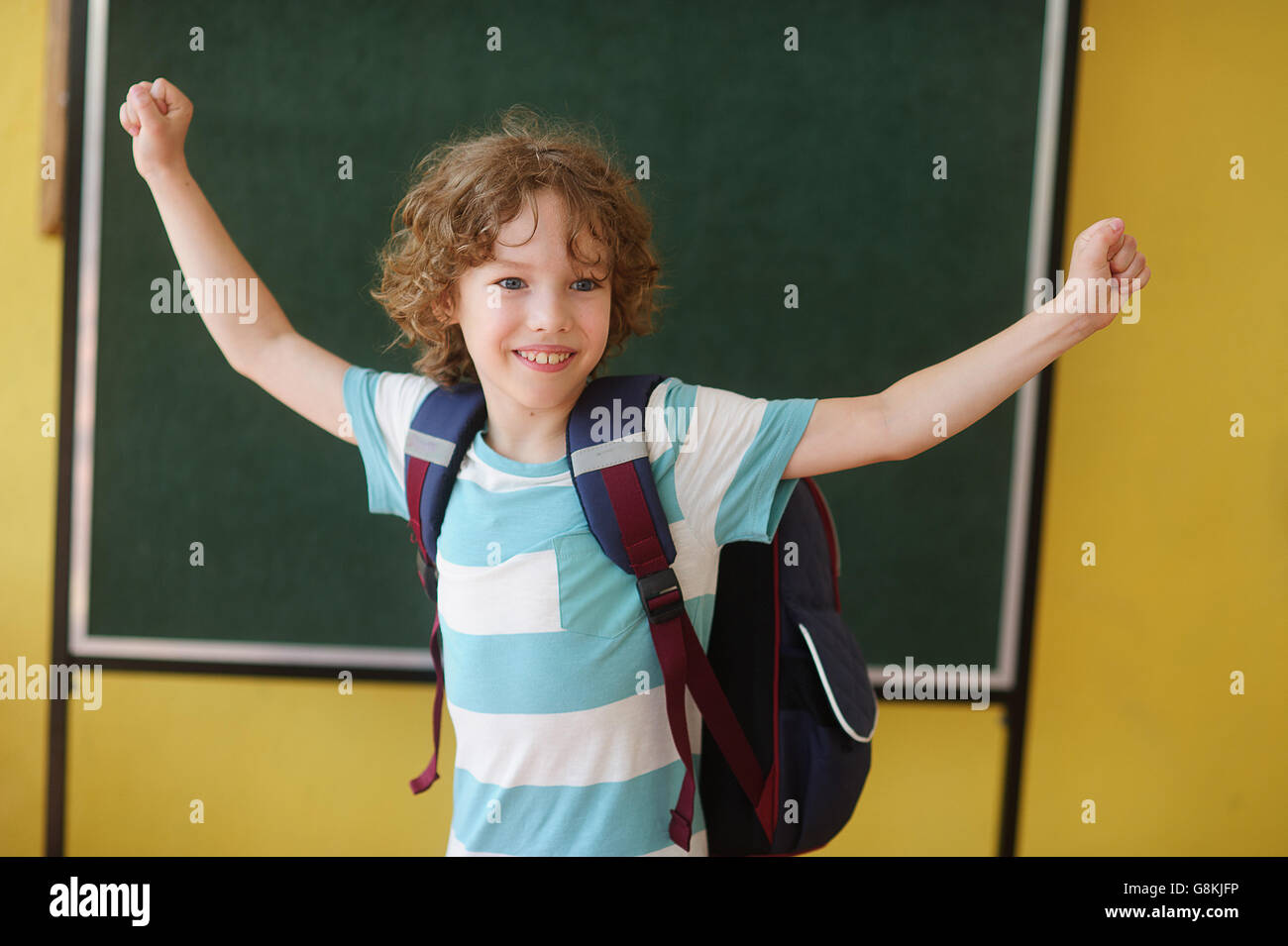 The fair-haired curly school student stand against a blackboard. The ...