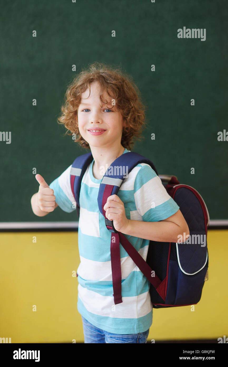 The cheerful pupil stands near a board in a class. He with a smile ...